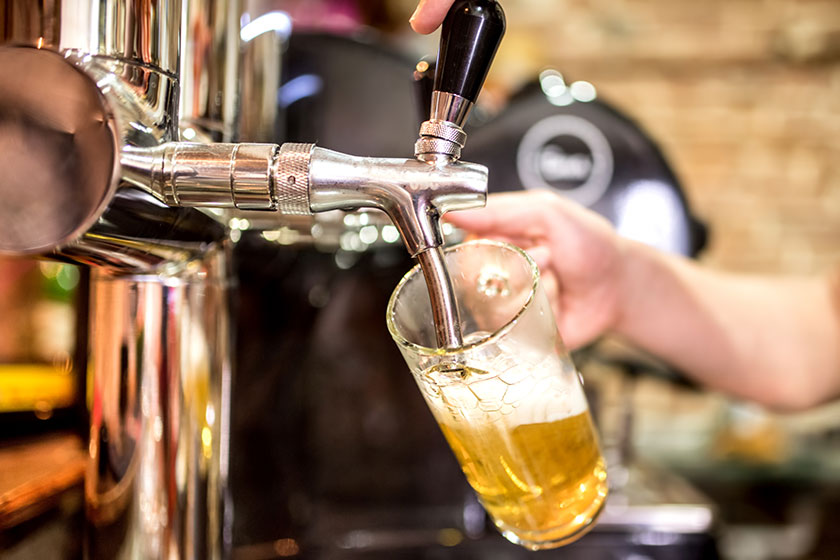 Barman hand at beer tap pouring a draught lager beer serving in a ...